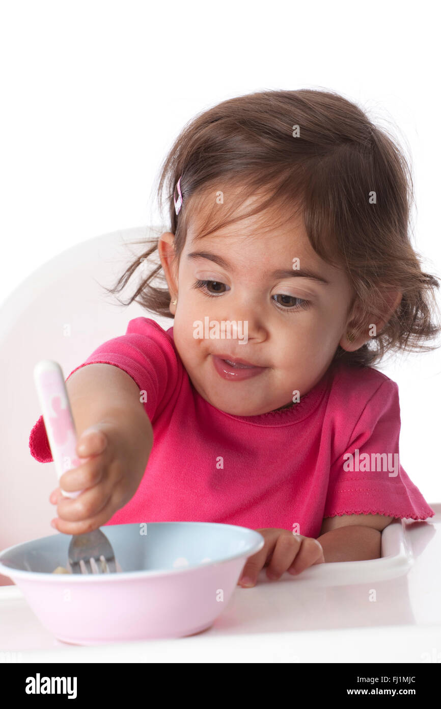 Baby girl is eating by herself on white background Stock Photo - Alamy
