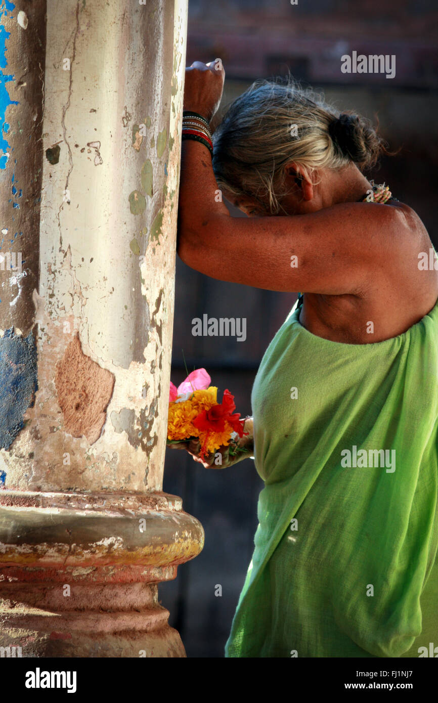 Woman leaning on a pillar with flowers for puja ritual in her hand ,in ...