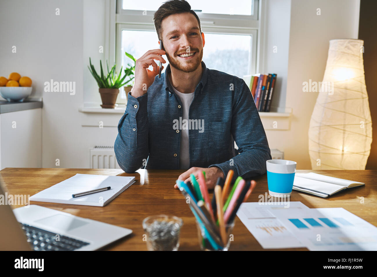 Smiling man working at desk office talking on phone looking at camera ...