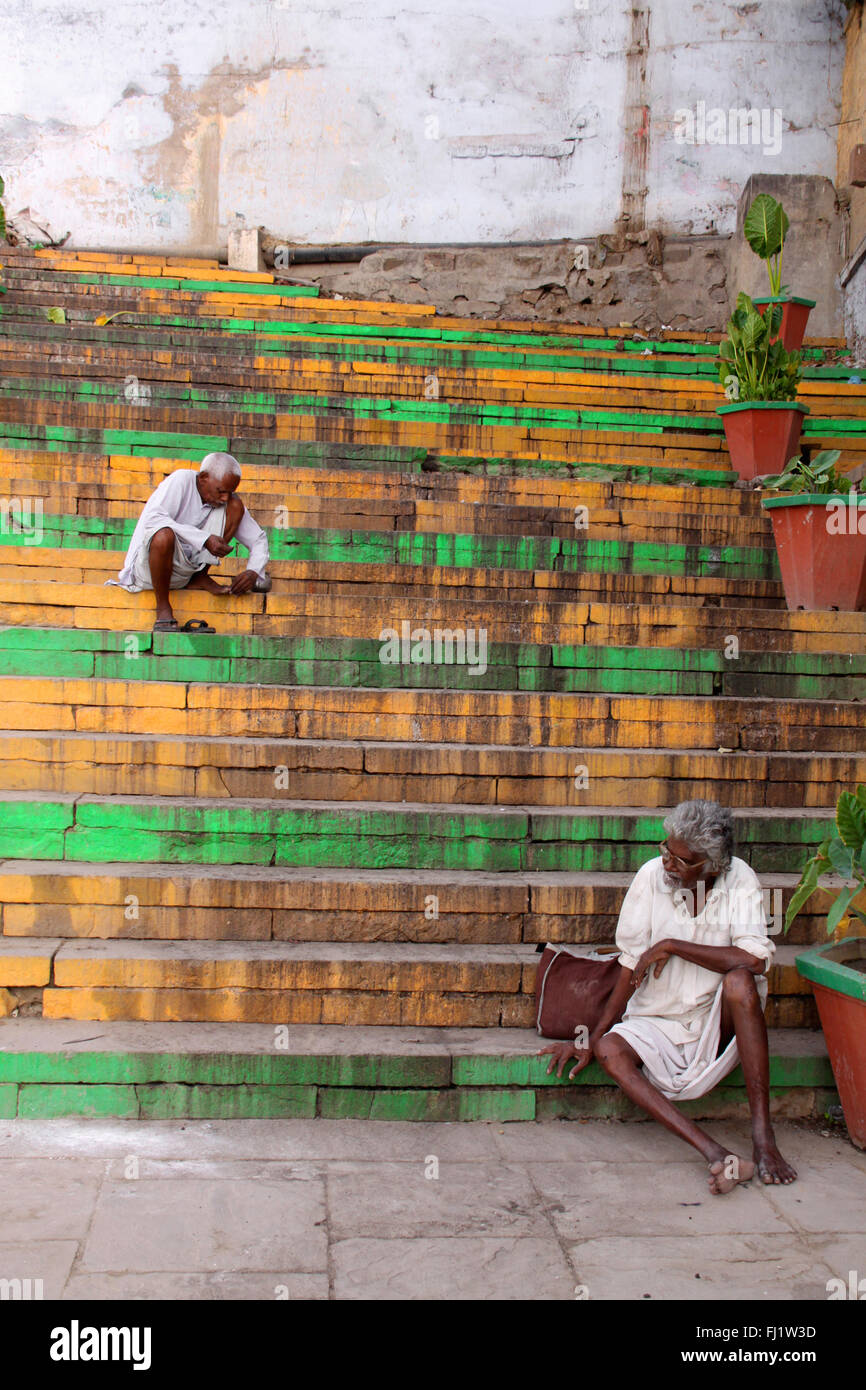 Two men sit on ghat in Varanasi with yellow and green colored steps ...
