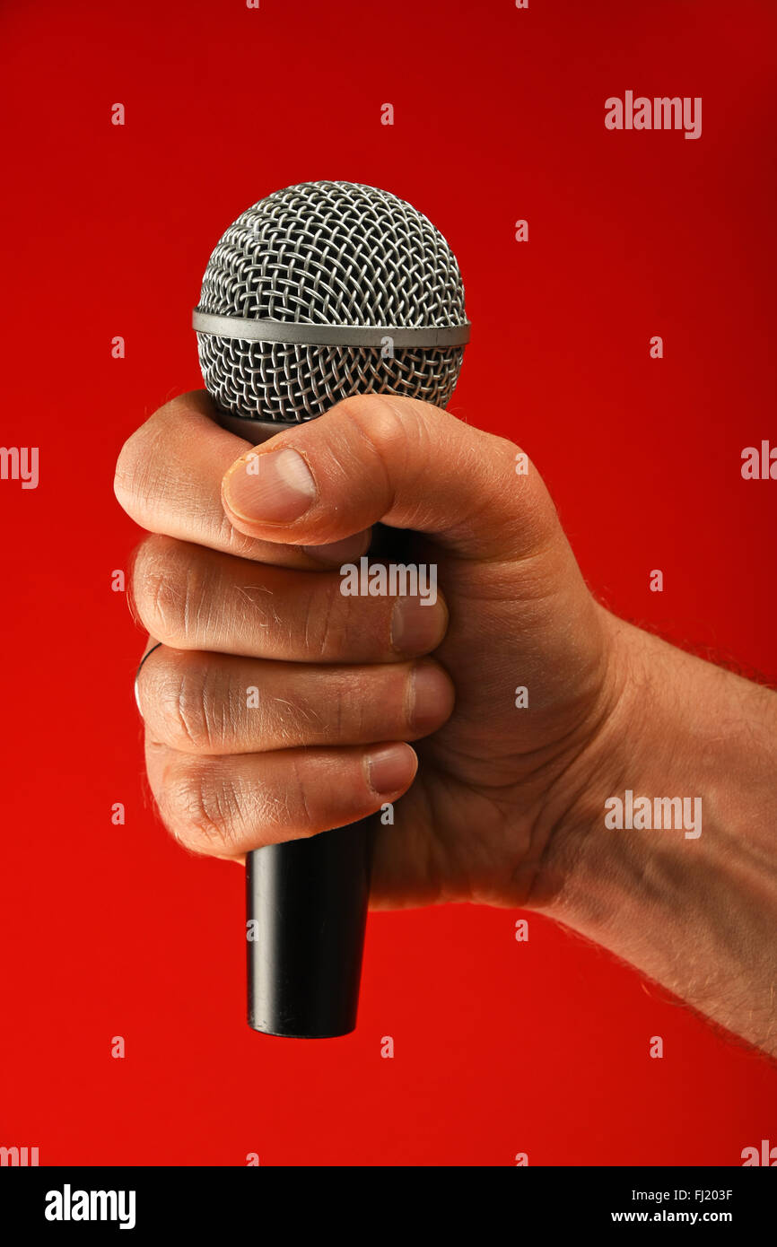 Man hand holding voice microphone in fist over red background Stock ...