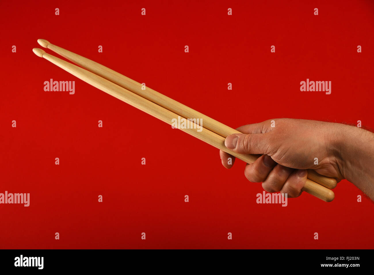 Man hand holding two wooden drumsticks over red background, diagonal ...
