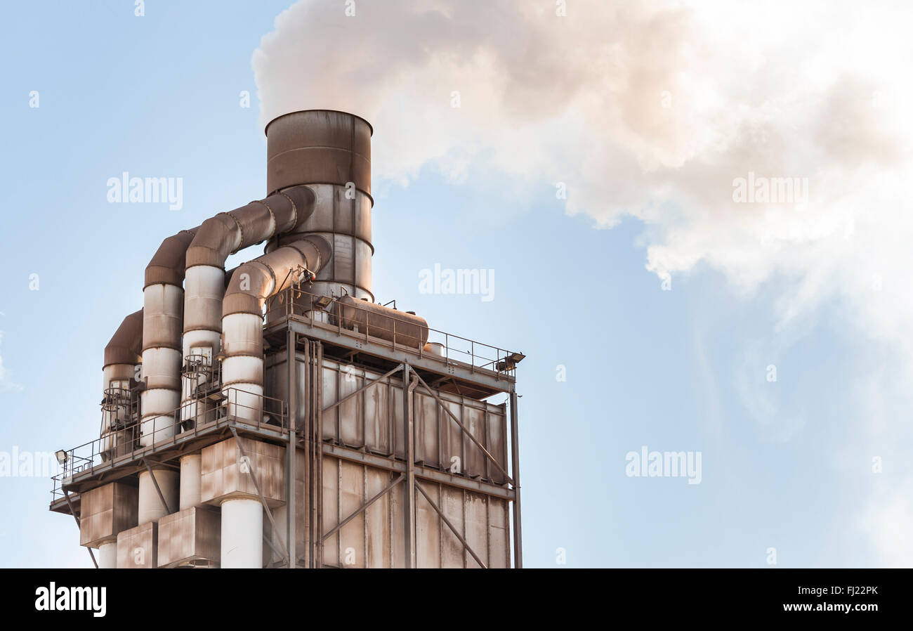 Old smokestack that emits white smoke in the clear blue sky Stock Photo ...