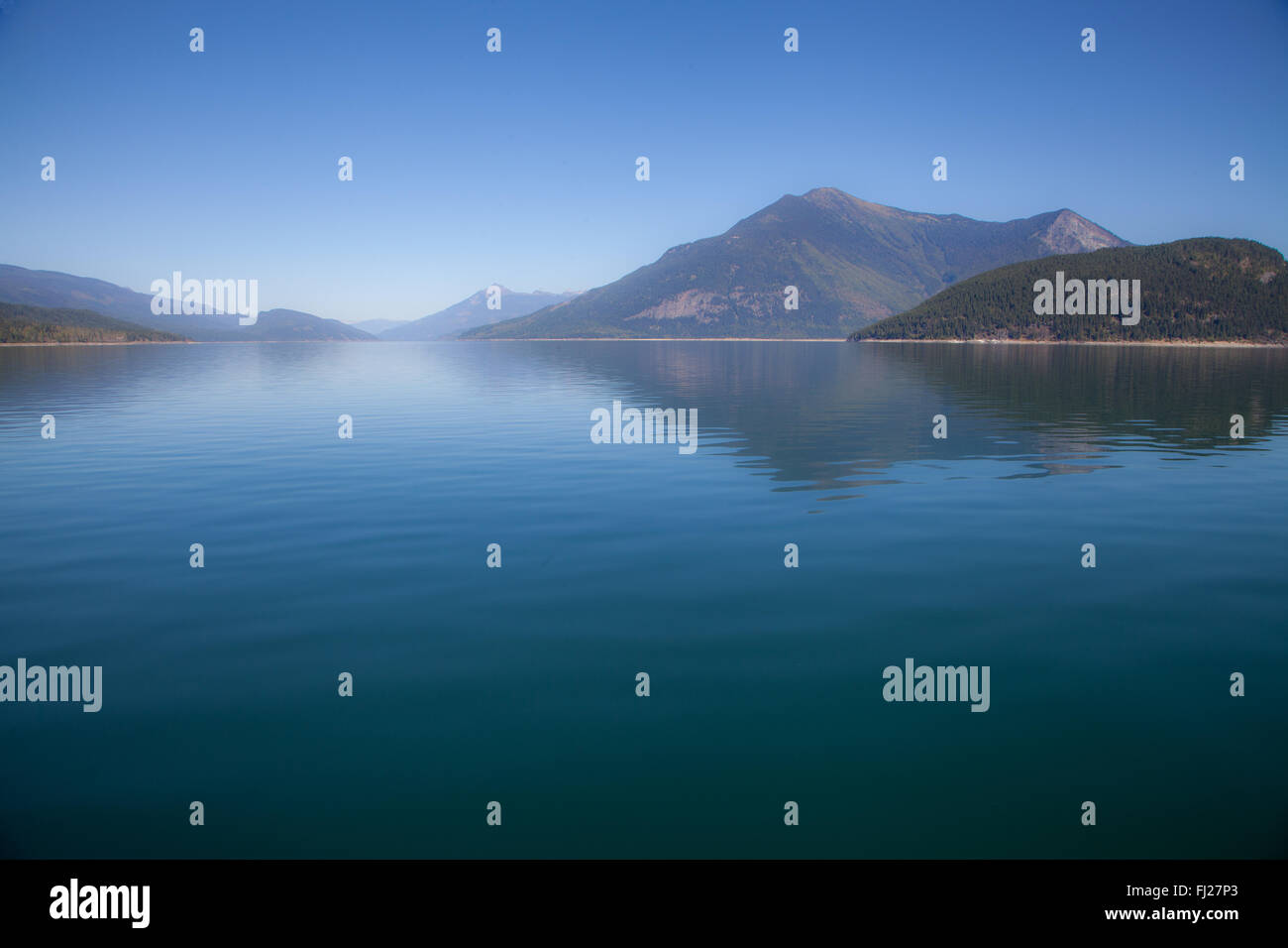 The blue water of Arrow Lake reflects the cloudless blue sky Kootney ...