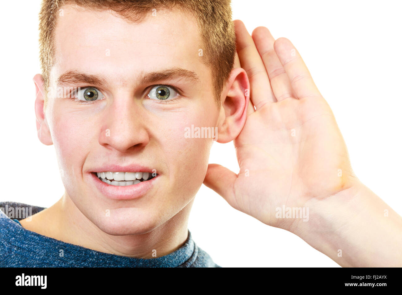 Gossip. Young man holding hand to ear listening isolated on white ...