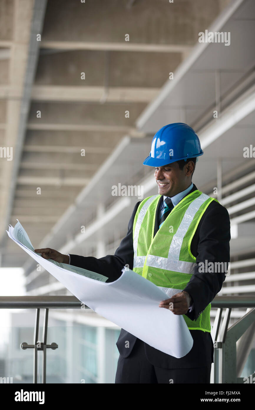 Portrait of a male Indian industrial engineer at work holding technical ...