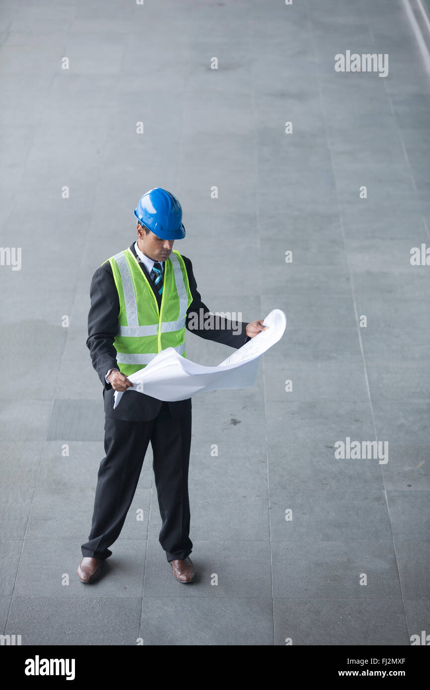 Portrait of a male Indian industrial engineer at work holding technical ...