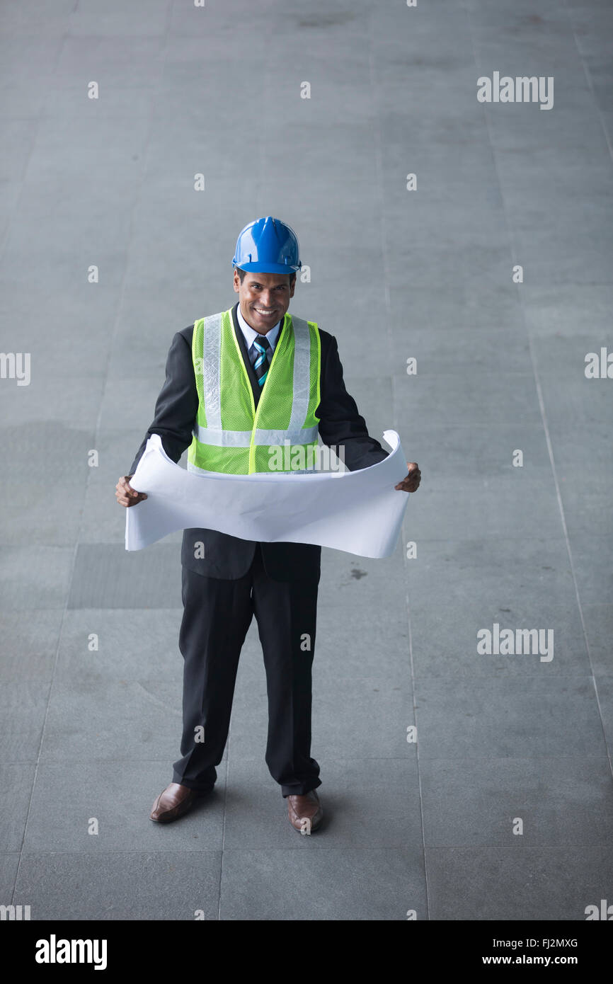 Portrait of a male Indian industrial engineer at work holding technical ...