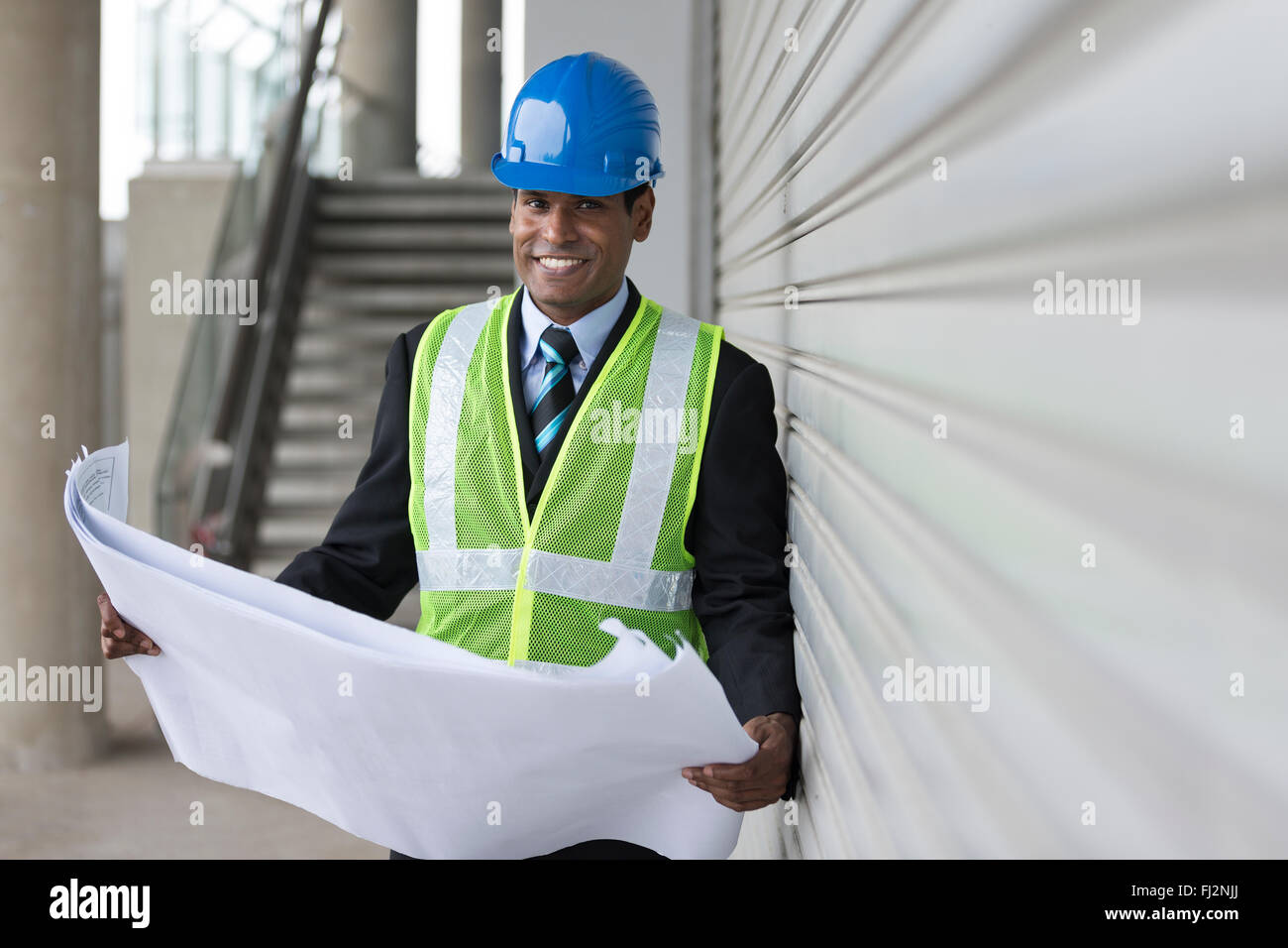 Portrait of a male Indian industrial engineer at work holding technical ...