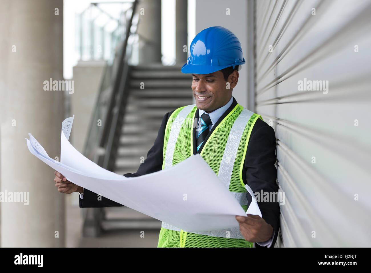 Portrait of a male Indian industrial engineer at work holding technical ...