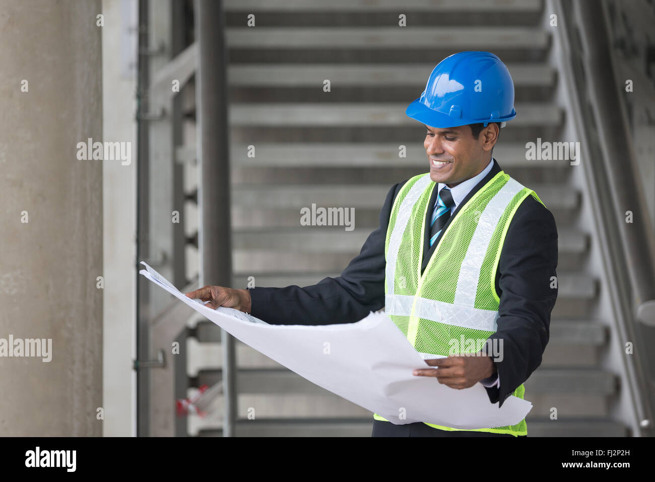 Portrait of a male Indian industrial engineer at work holding technical ...