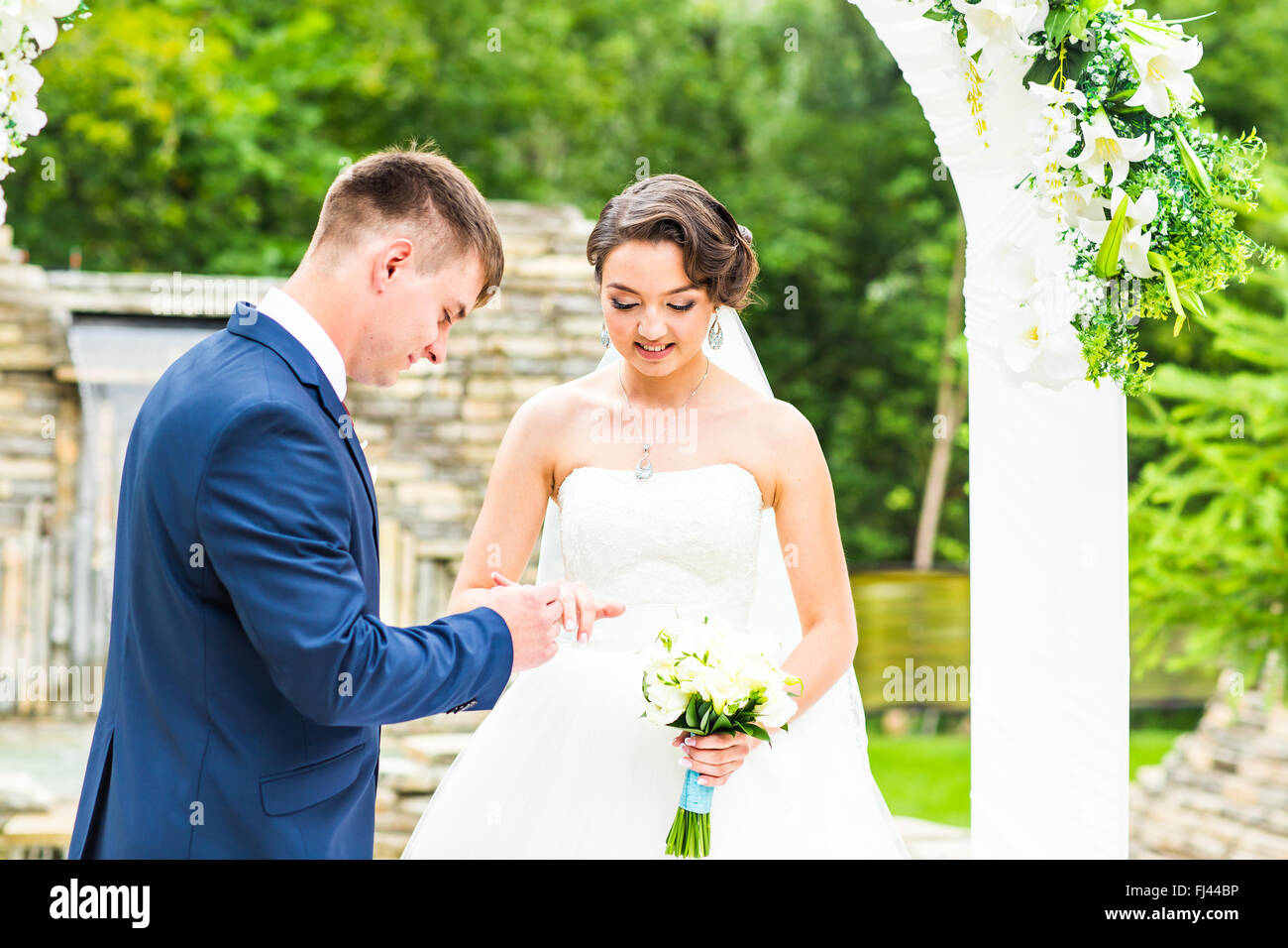 Groom slipping ring on finger of bride at wedding Stock Photo - Alamy
