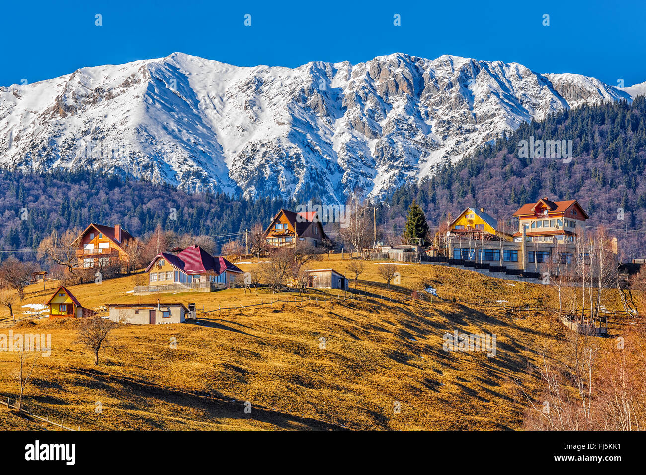 Snowy Piatra Craiului mountain ridge and scattered houses uphill in ...