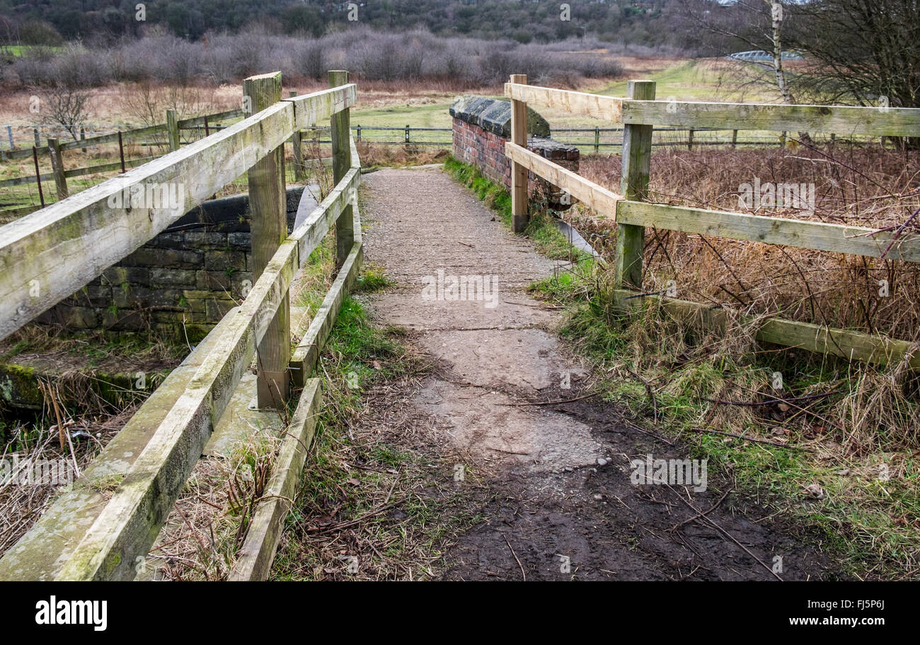 A small footpath leading to a bridge over the canal with wooden fences ...
