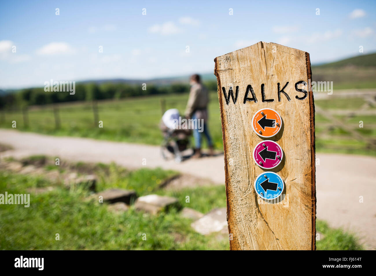 A woman walks past a wooden sign for walks in the Peak District on a ...
