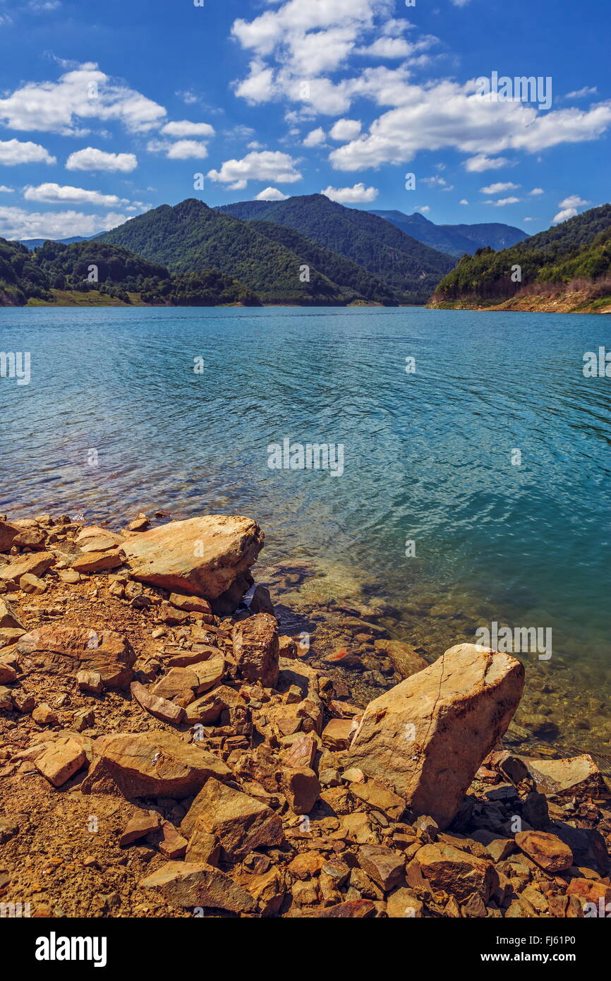 Peaceful scenery of a wide mountain lake with rocky shore and limpid ...