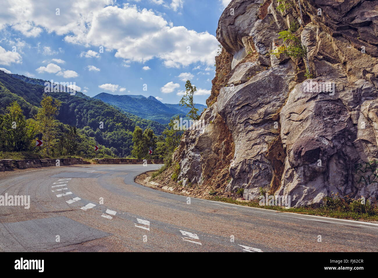 Sunny summer view with steep rocky cliff on the side of a road crossing ...