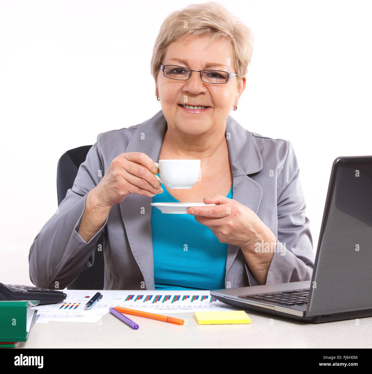 Elderly senior business woman drinking tea or coffee at her desk in ...