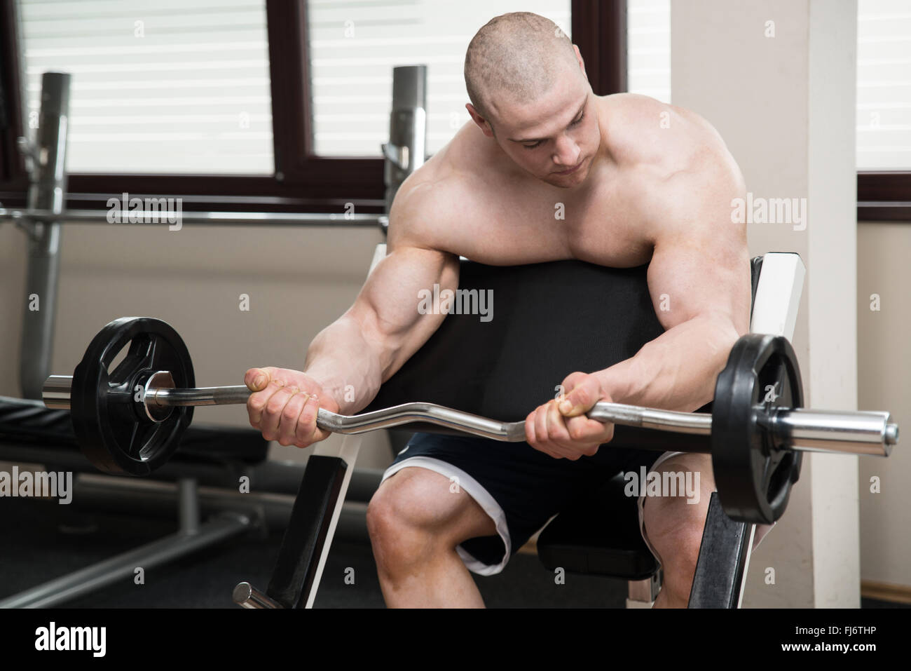 Muscular Man Doing Heavy Weight Exercise For Biceps With Barbell In Gym ...