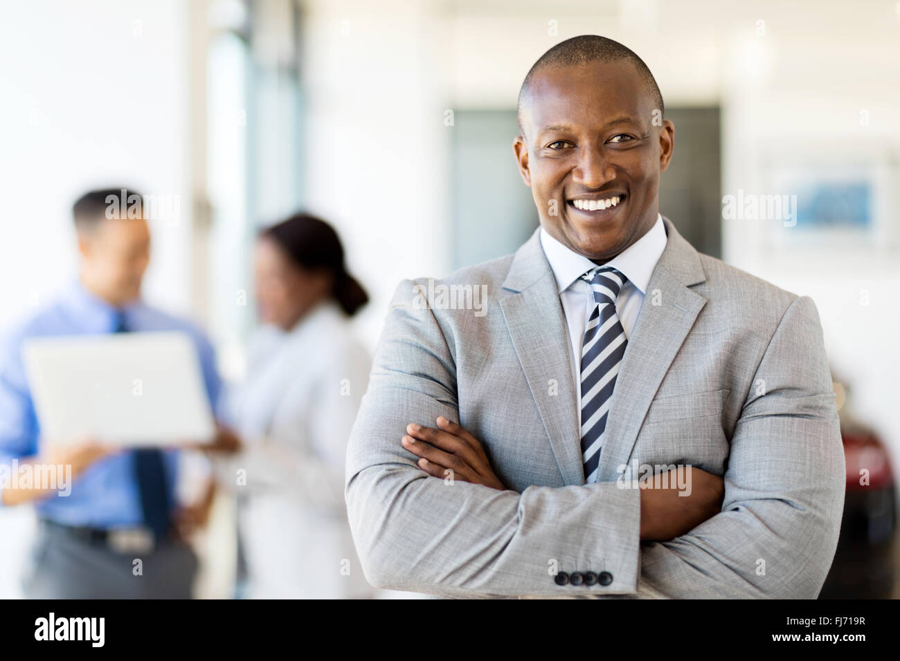 happy African salesman standing at car dealership with colleagues on ...