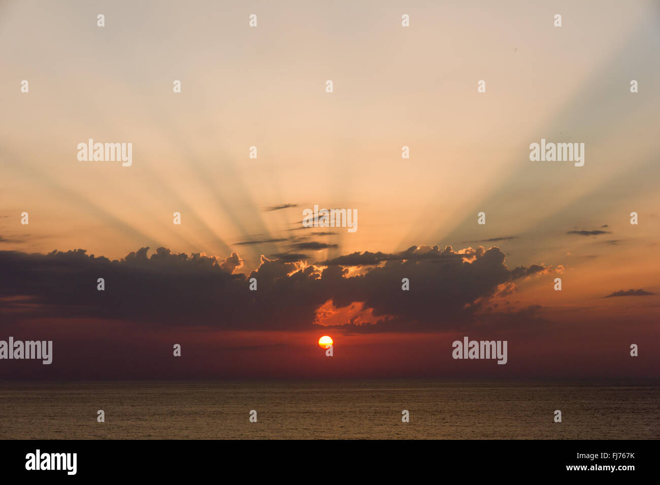 sunset over the ocean with visible sunshine over the clouds Stock Photo ...