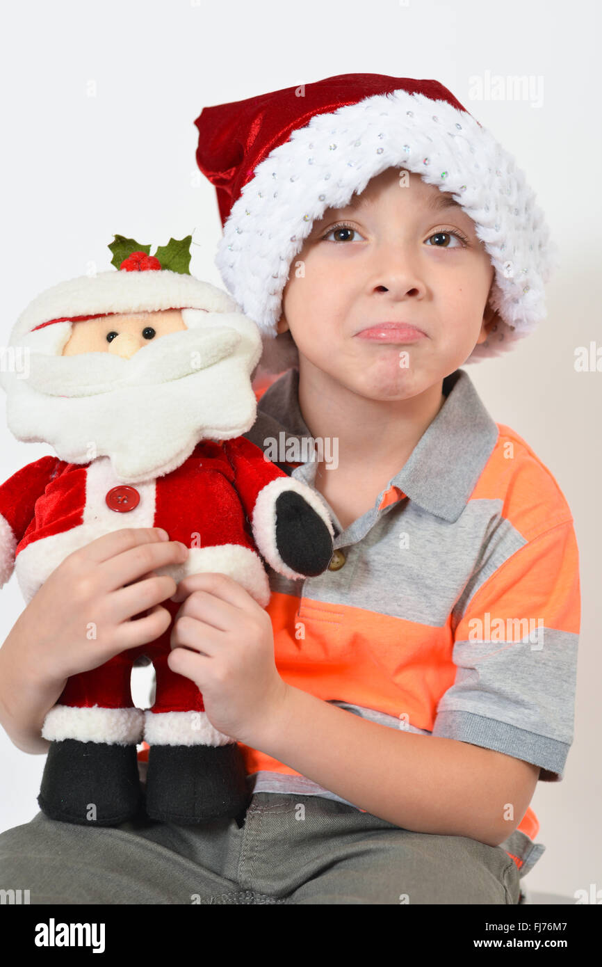 Adorable boy holding a Santa Claus toy while wearing a Christmas hat ...