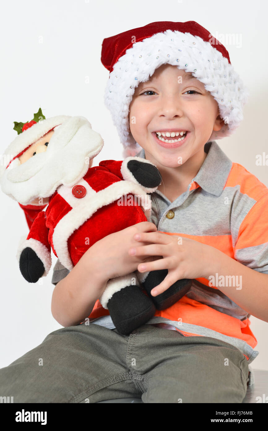 Adorable boy holding a Santa Claus toy while wearing a Christmas hat ...