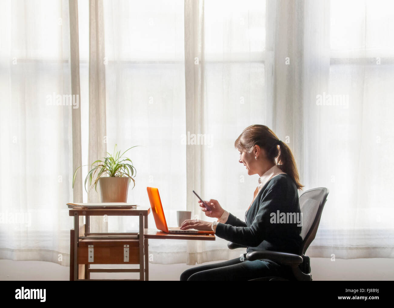 A woman sitting at a computer with window behind her Stock Photo - Alamy