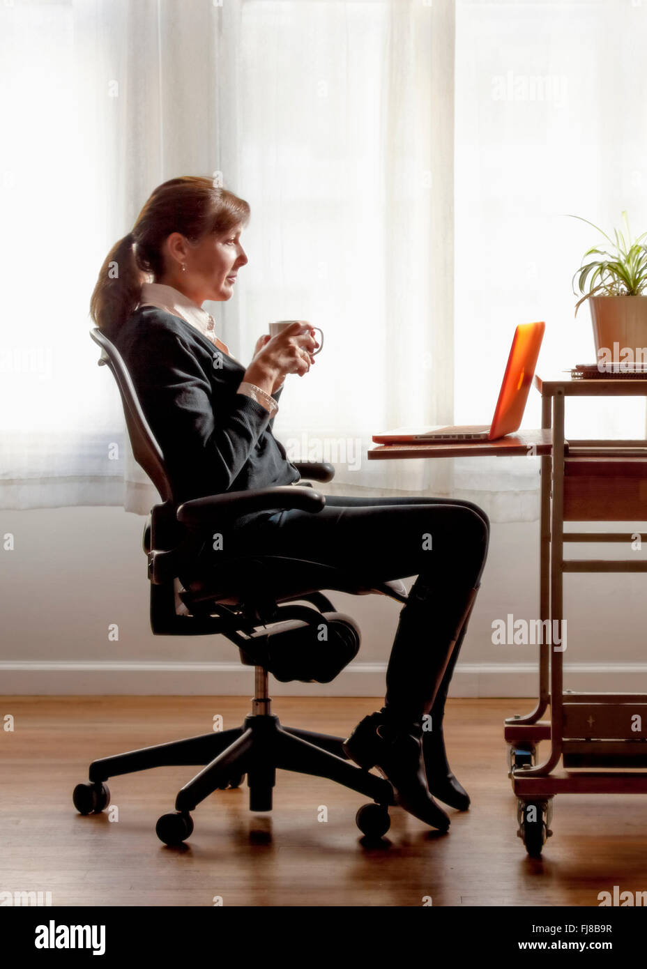 A woman sitting at a computer with window behind her Stock Photo - Alamy