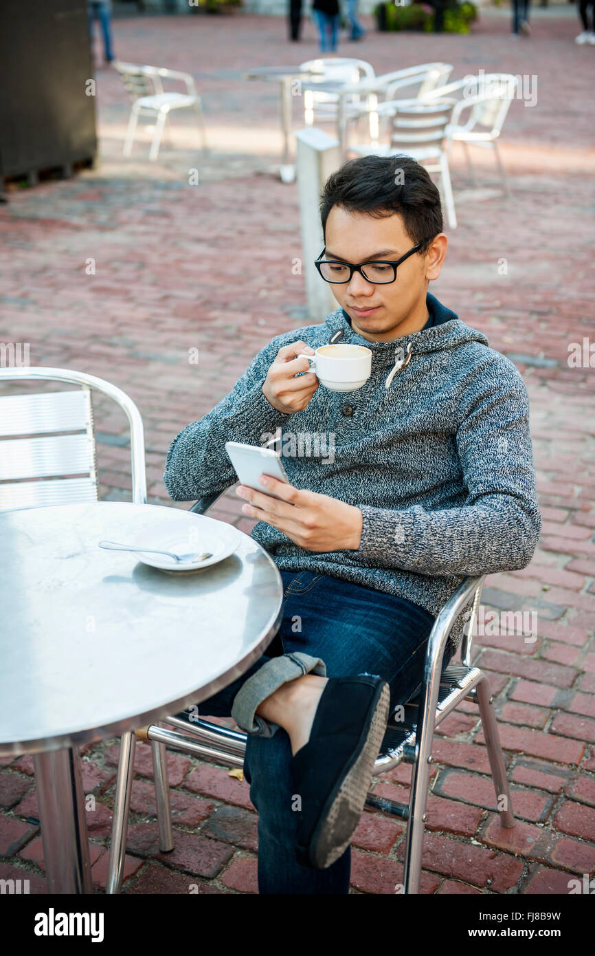 Serious young asian man sitting in relaxing outdoor cafe holding cup of ...
