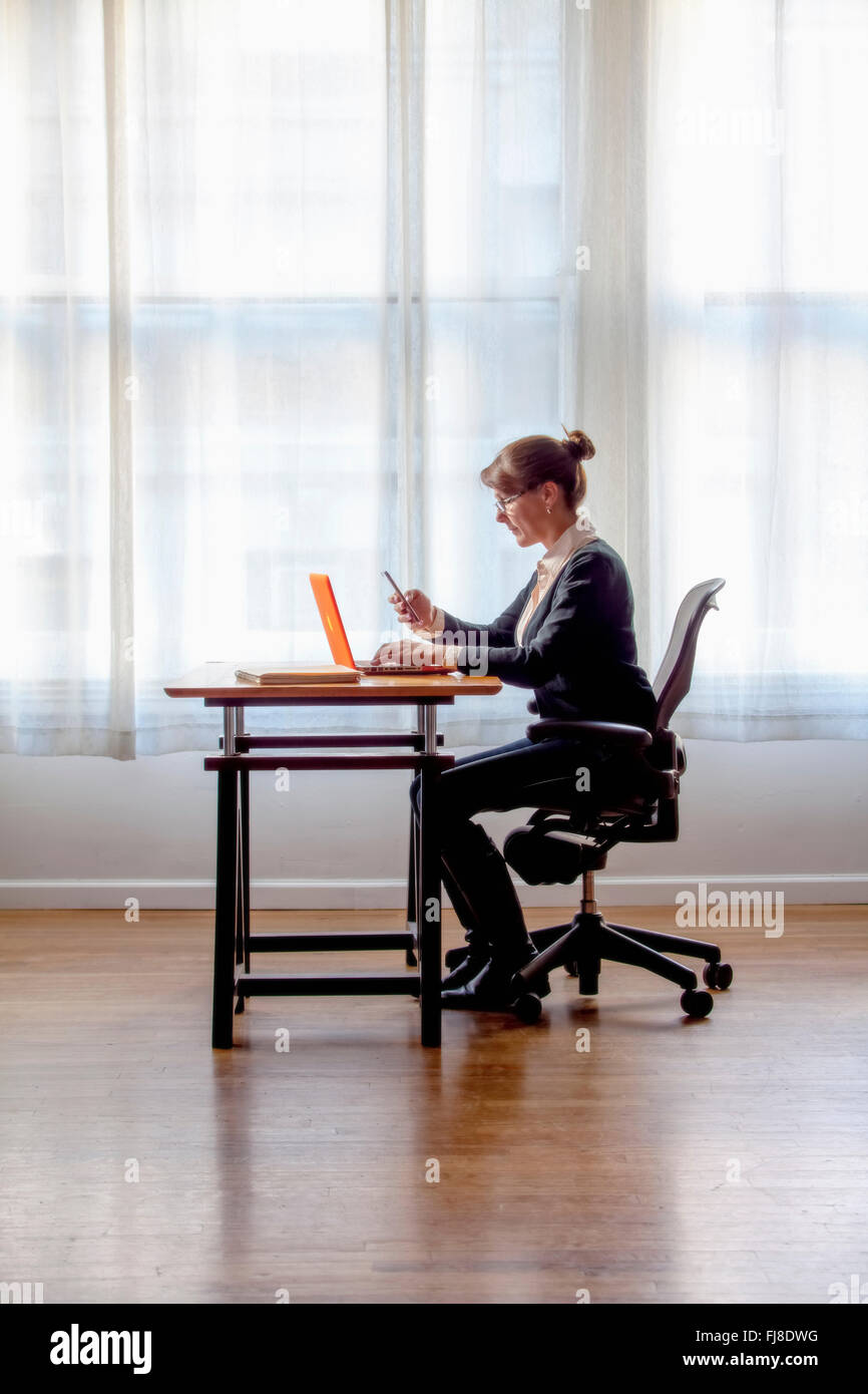 A woman sitting at a computer with window behind her Stock Photo - Alamy