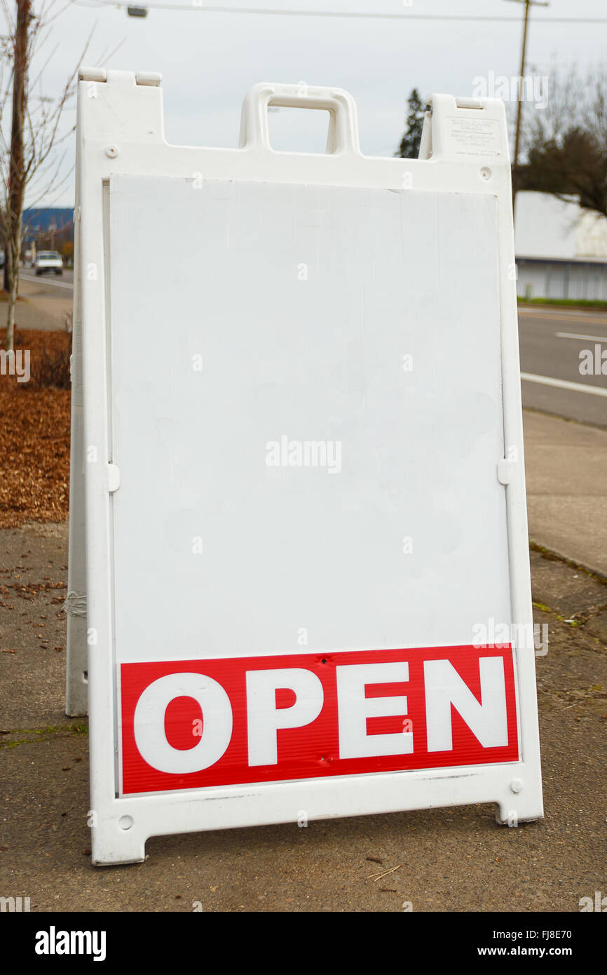 Blank white sign says open place on the sidewalk near a busy street in ...