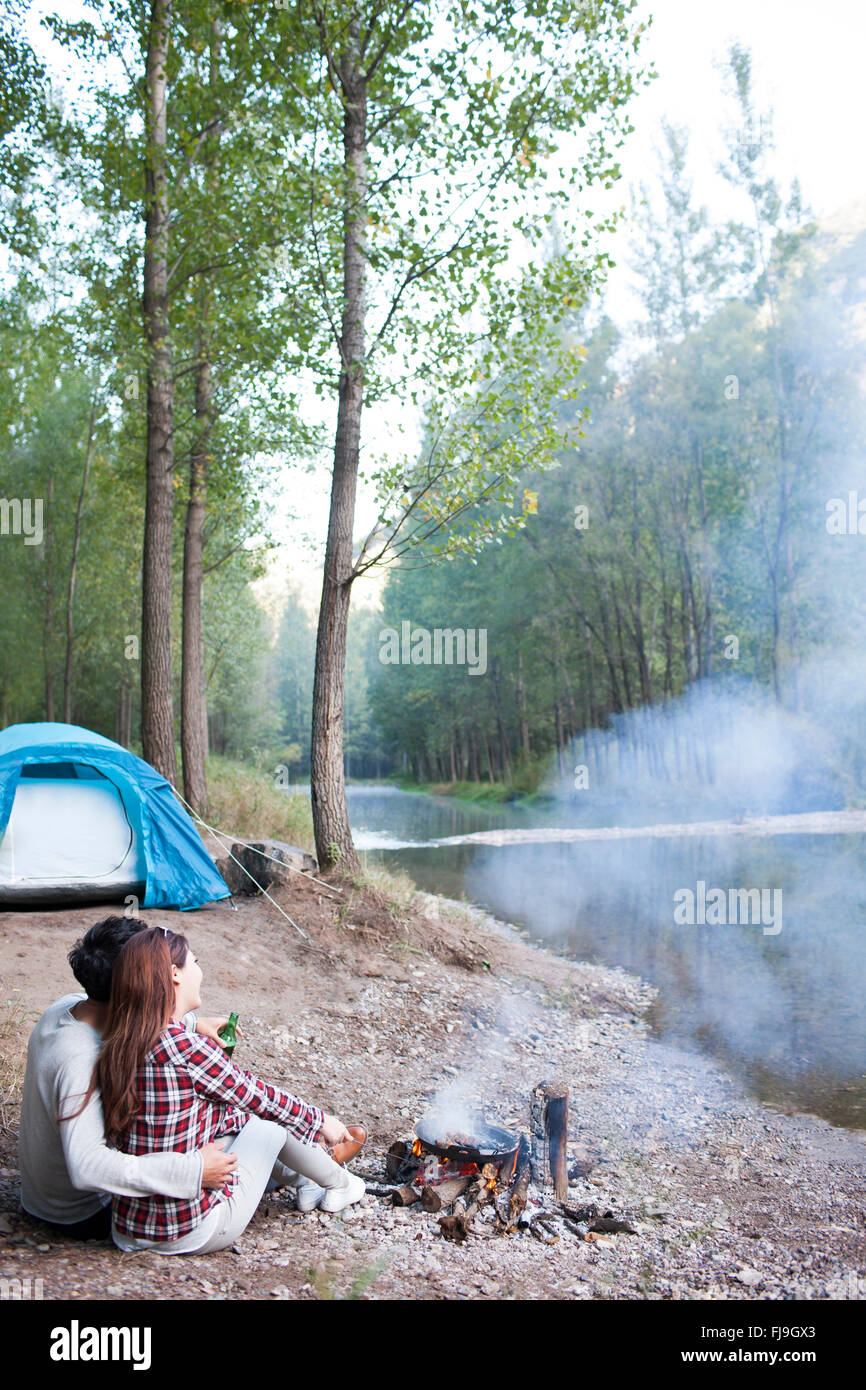 Young Chinese couple sitting beside campfire preparing food Stock Photo ...