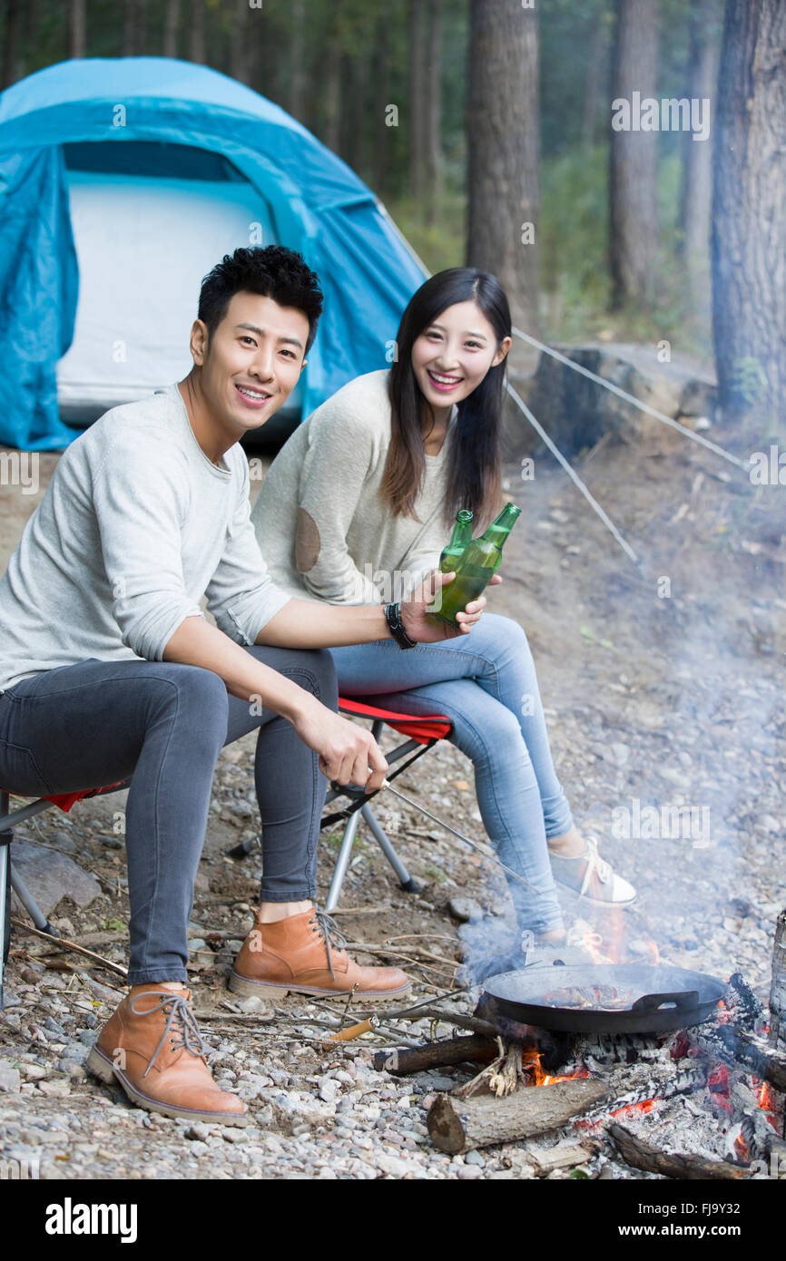 Young Chinese couple sitting beside campfire preparing food Stock Photo ...