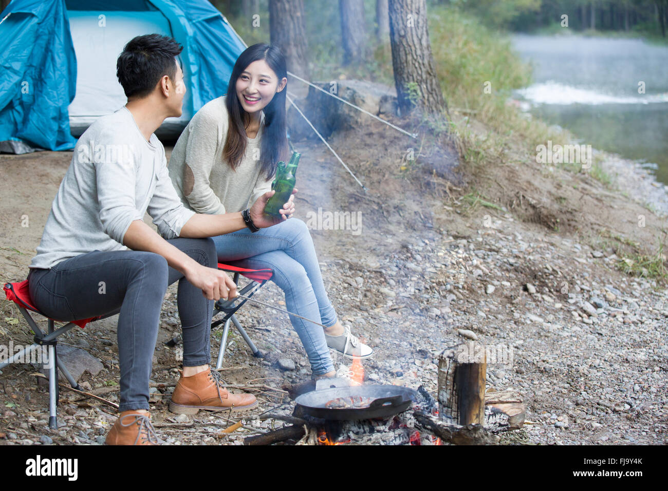 Young Chinese couple sitting beside campfire preparing food Stock Photo ...
