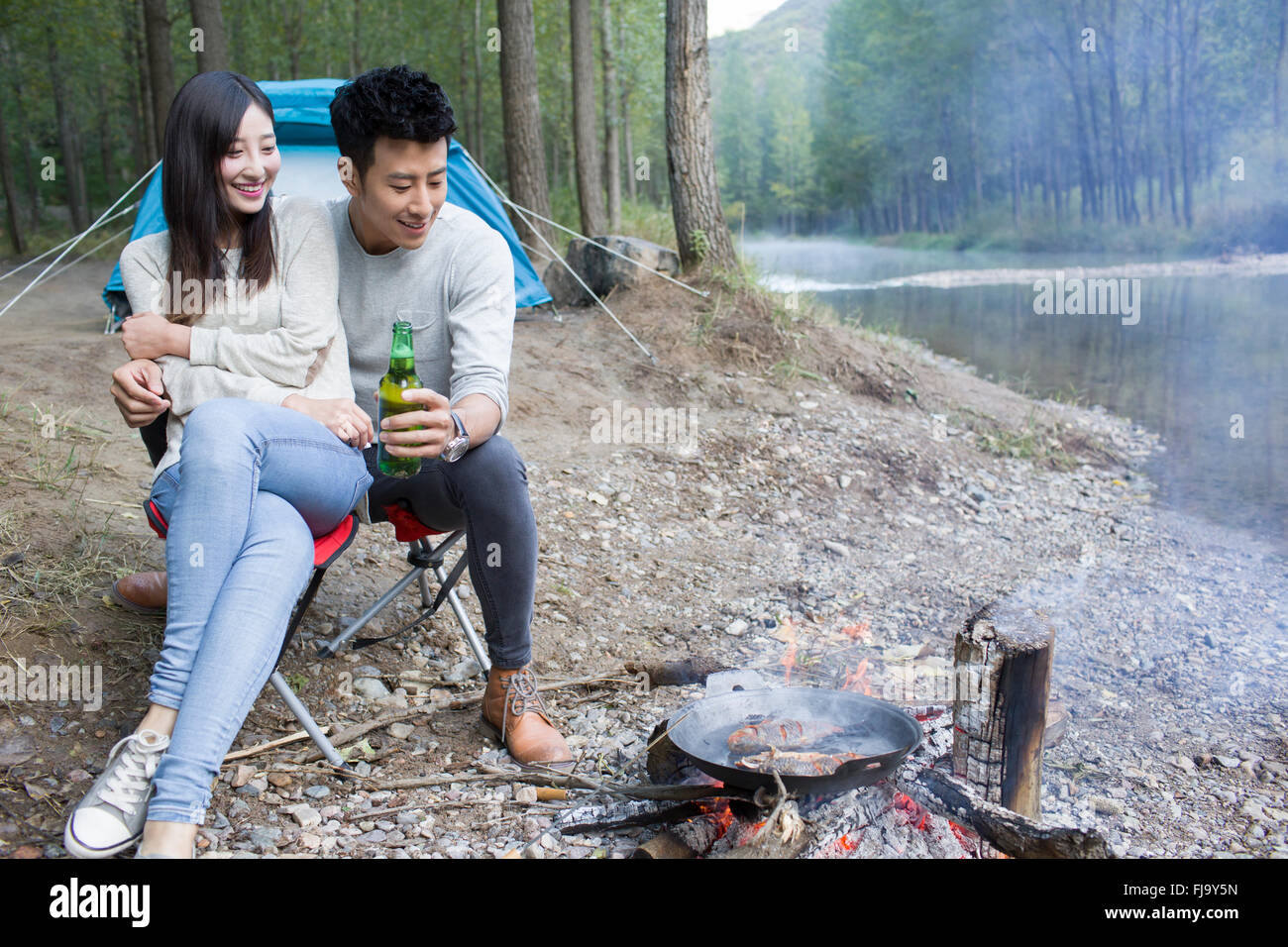 Young Chinese couple sitting beside campfire preparing food Stock Photo ...