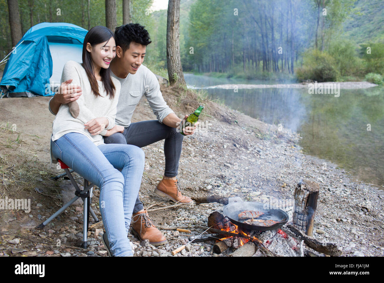 Young Chinese couple sitting beside campfire preparing food Stock Photo ...