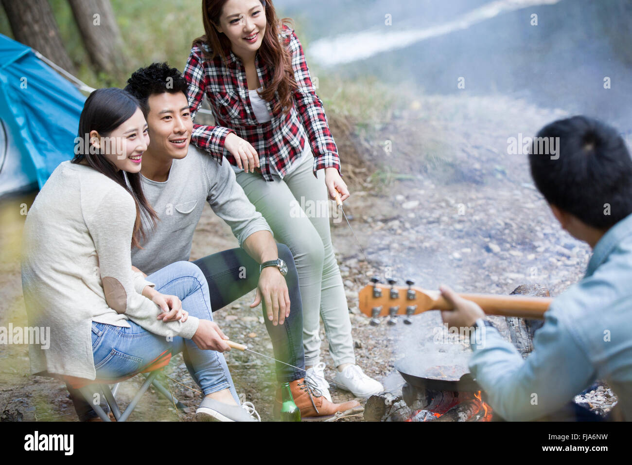 Young Chinese friends sitting around campfire playing guitar Stock ...