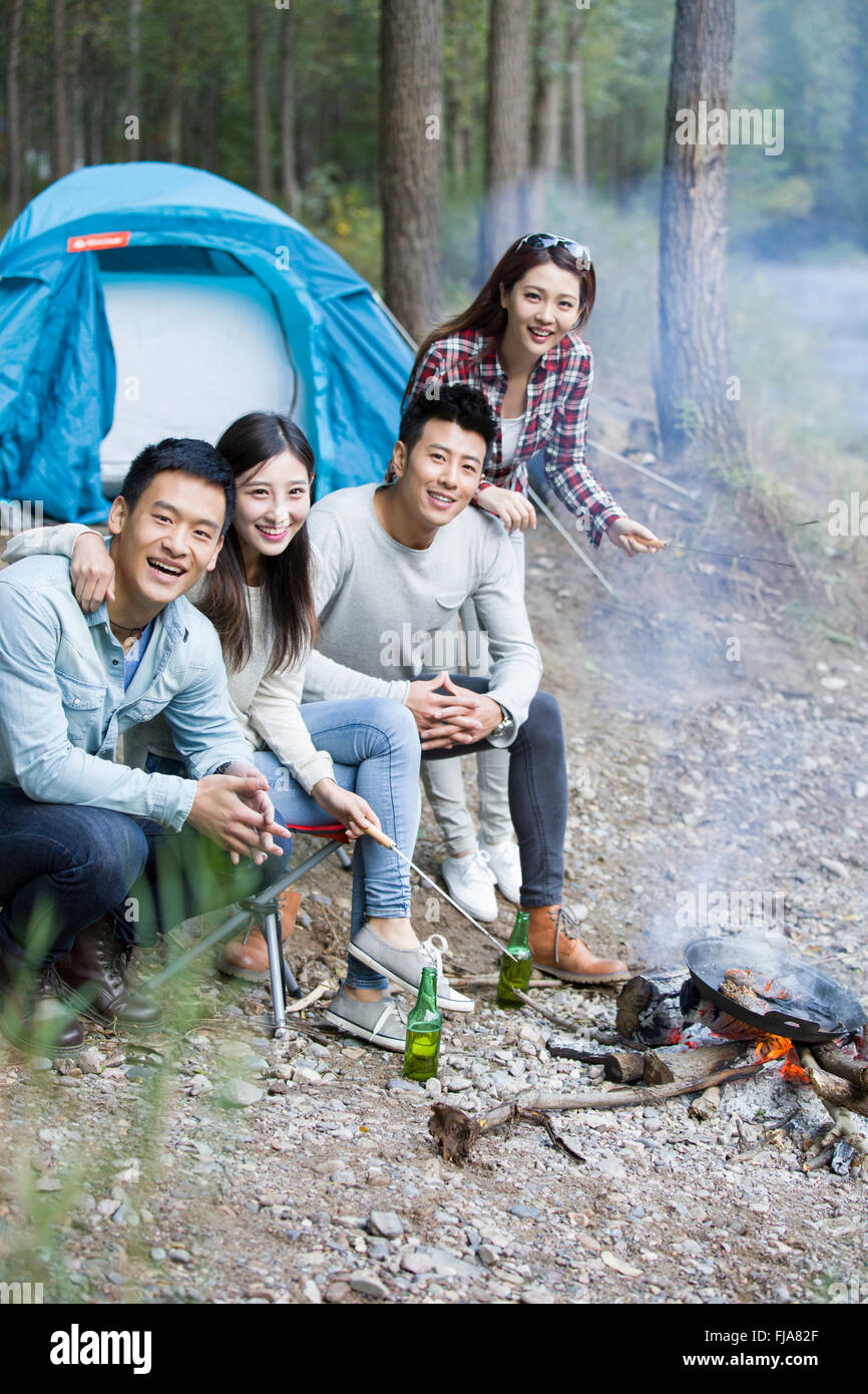 Young Chinese friends sitting beside campfire preparing food Stock ...