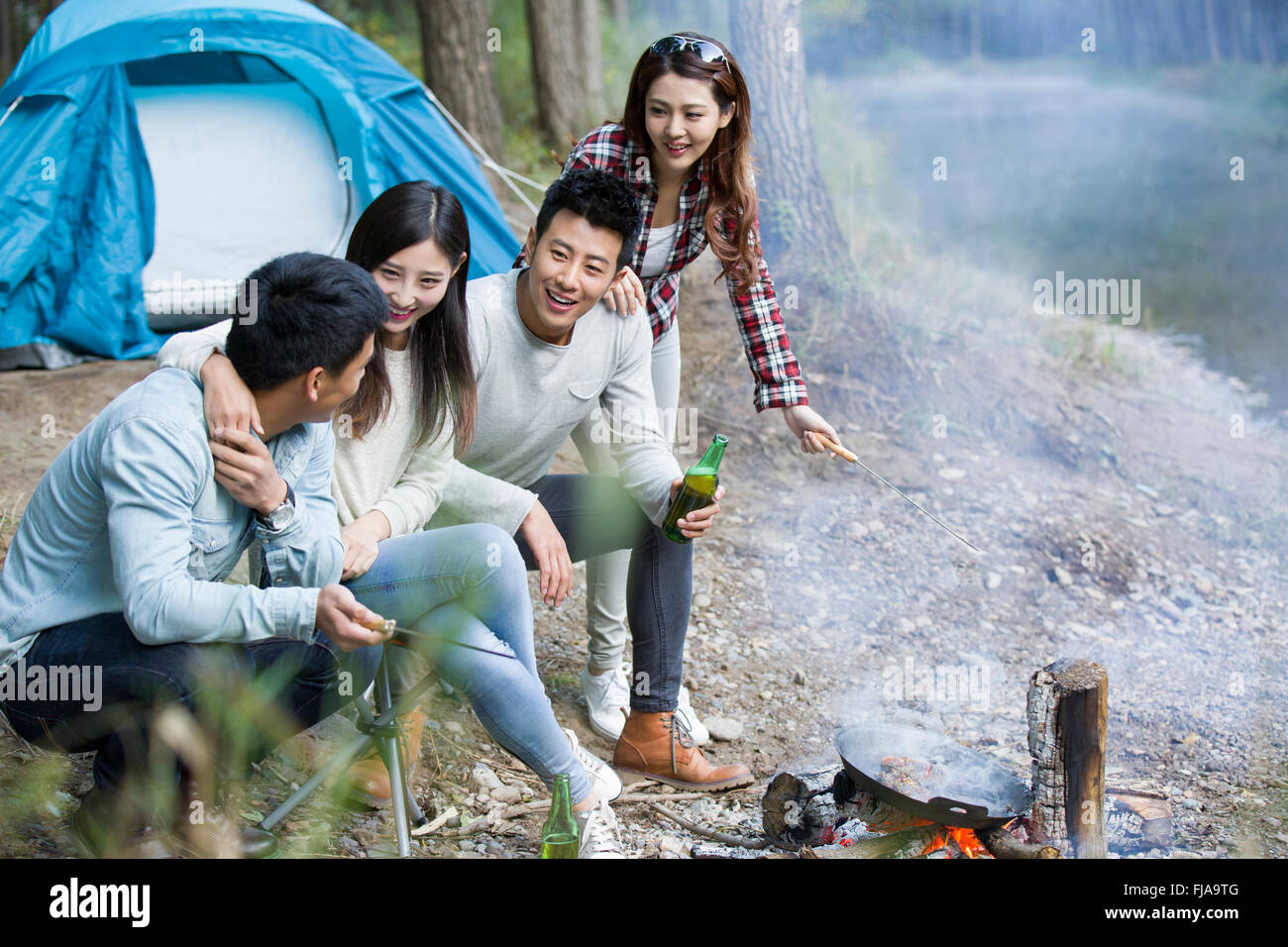 Young Chinese friends sitting beside campfire preparing food Stock ...