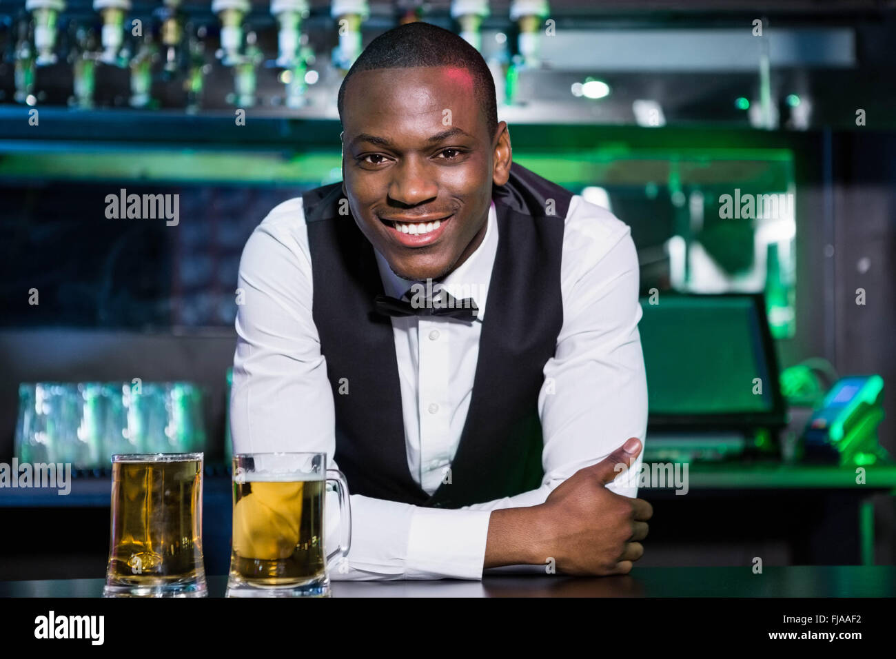 Bartender leaning on bar counter with two glasses of beer in front of ...