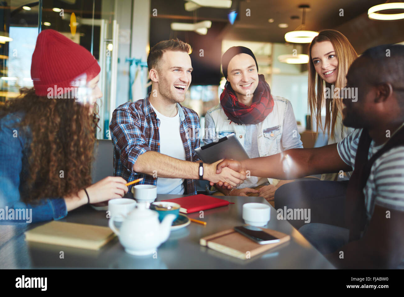 Young guys handshaking among their happy friends Stock Photo - Alamy