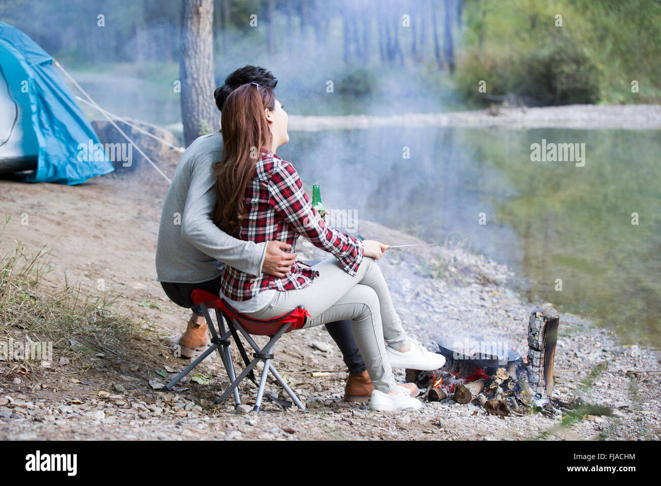 Young Chinese couple sitting beside campfire preparing food Stock Photo ...