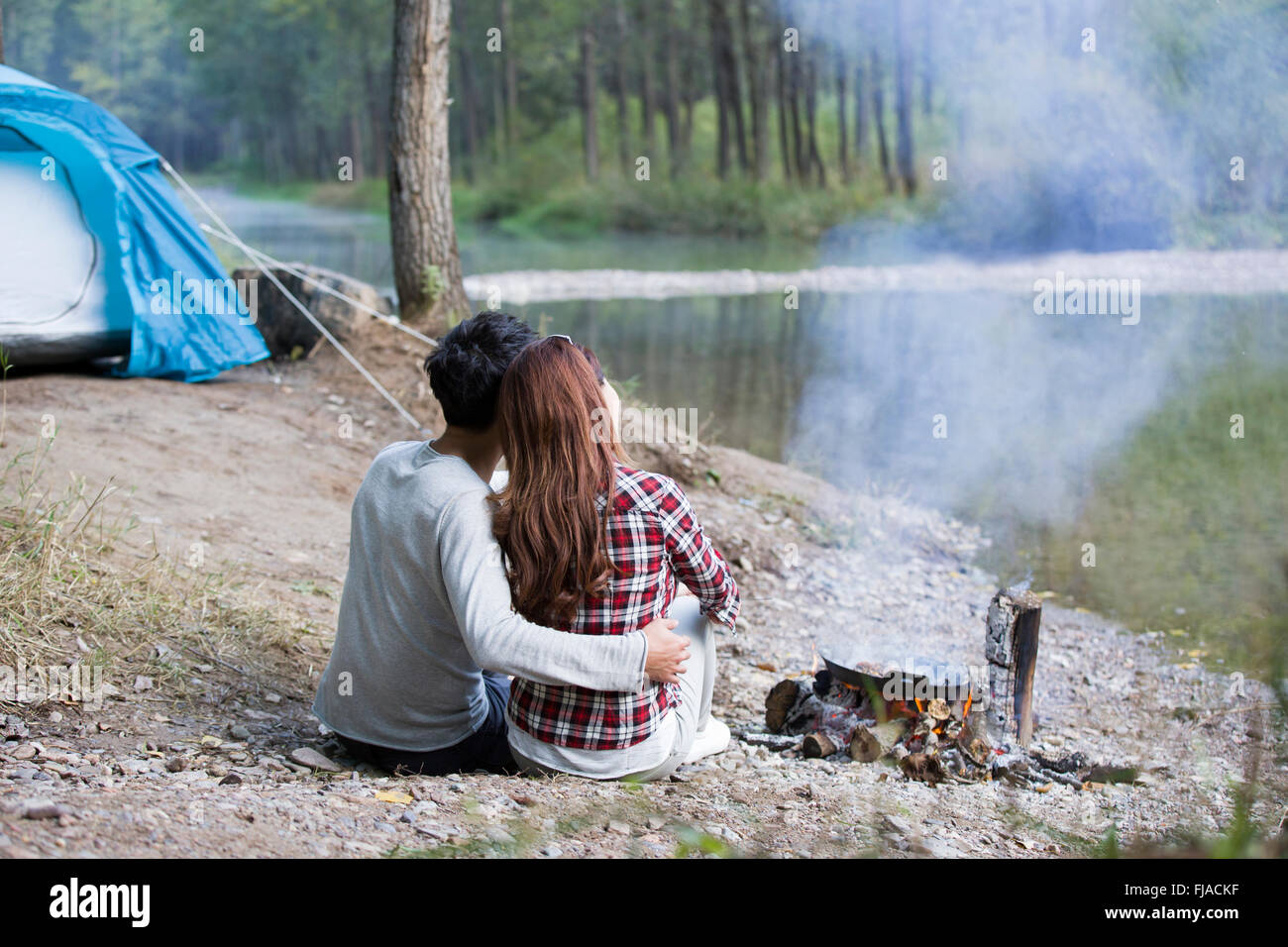 Young Chinese couple sitting beside campfire preparing food Stock Photo ...