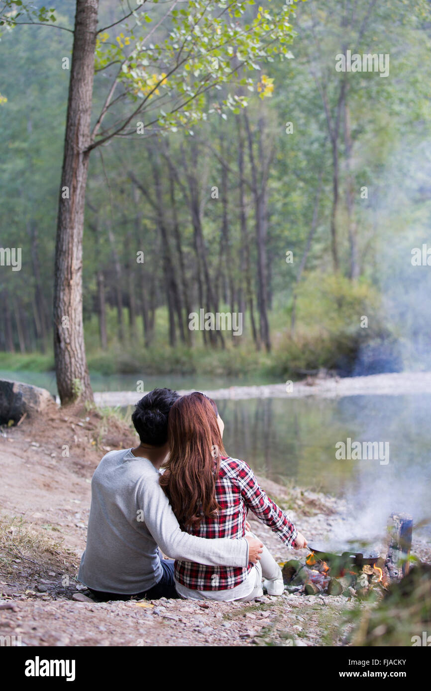 Young Chinese couple sitting beside campfire preparing food Stock Photo ...