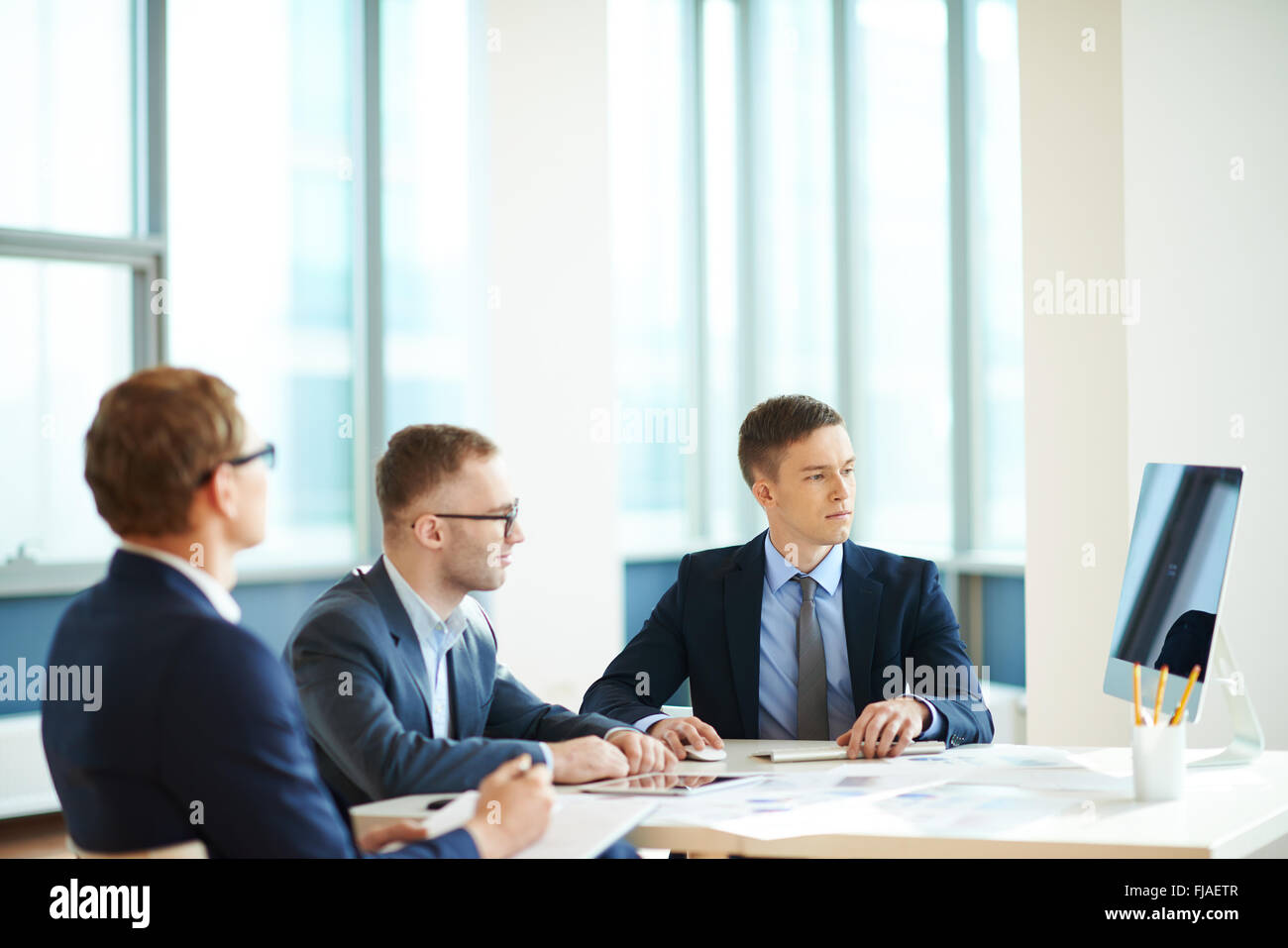 Three confident businessmen sitting in front of pc in office Stock ...
