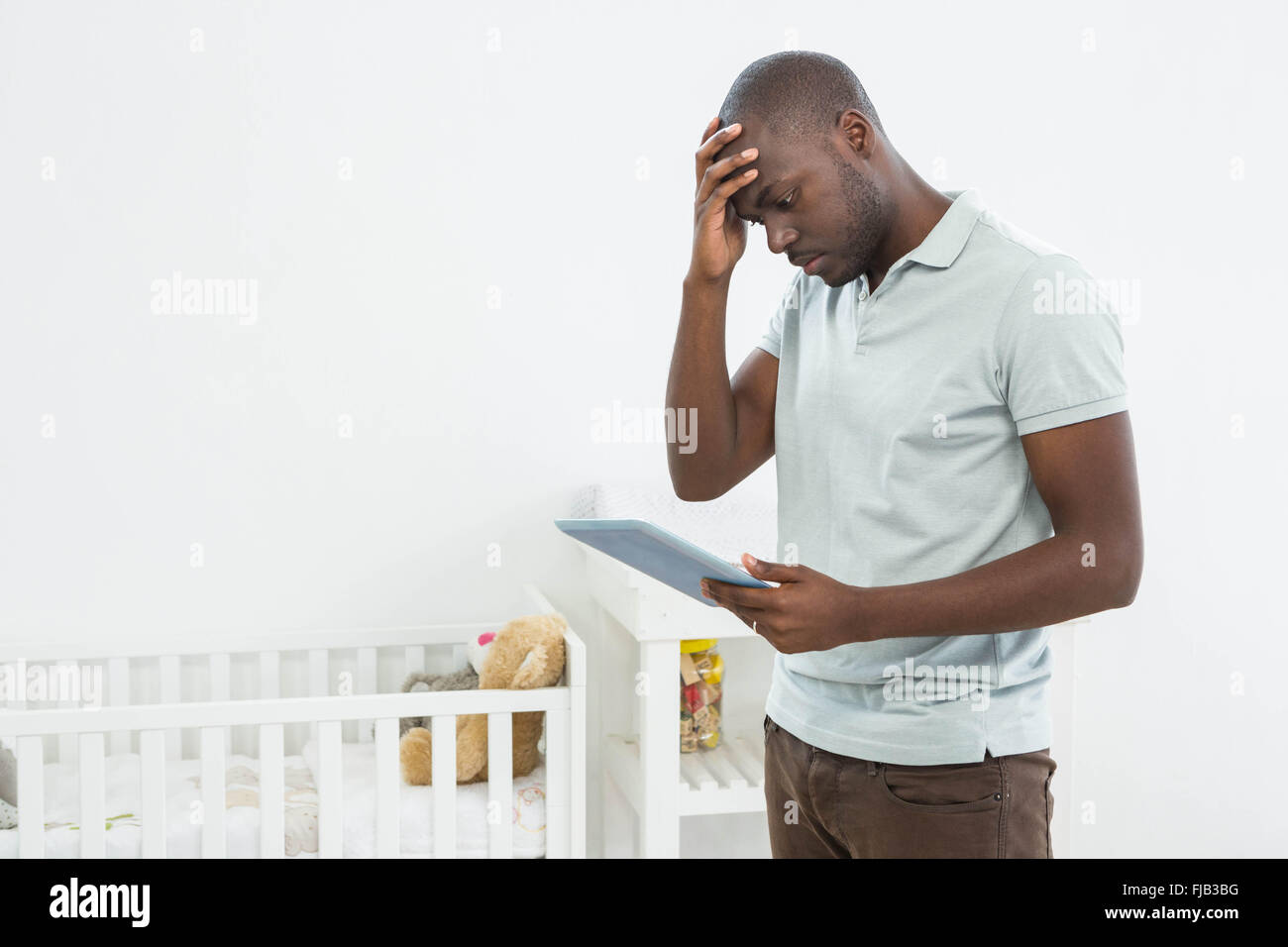 Tensed man standing next to a cradle and using digital tablet Stock ...