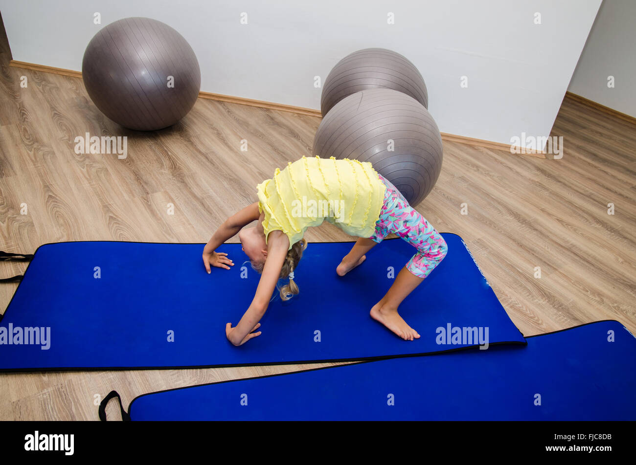 little blond girl in gym doing bridge posture over blue matt Stock ...