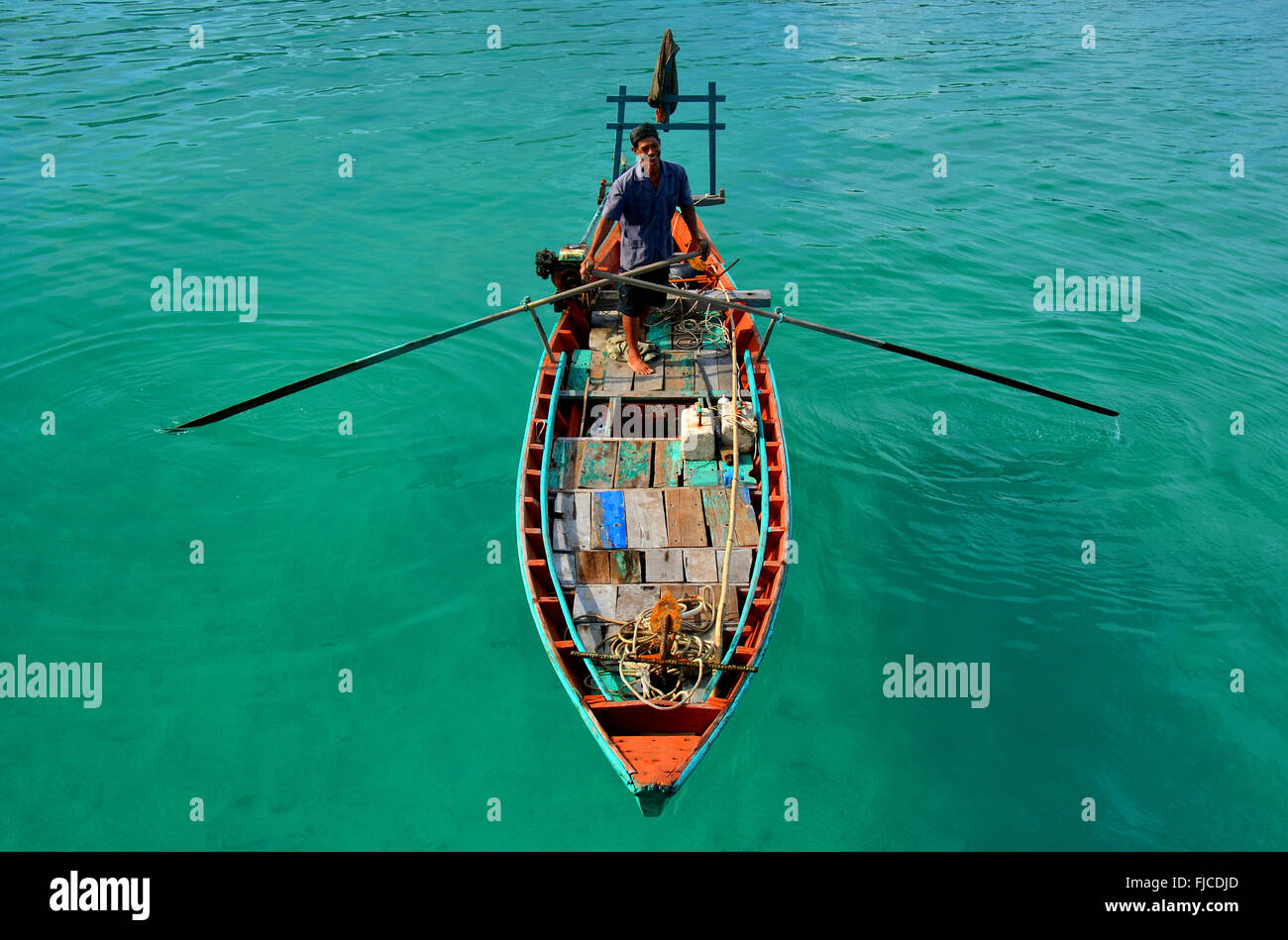 A Cambodian man happily rowing his boat next to the beautiful island ...