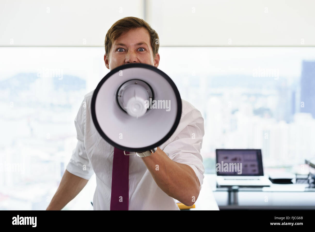 Portrait of furious business man screaming with megaphone in modern ...
